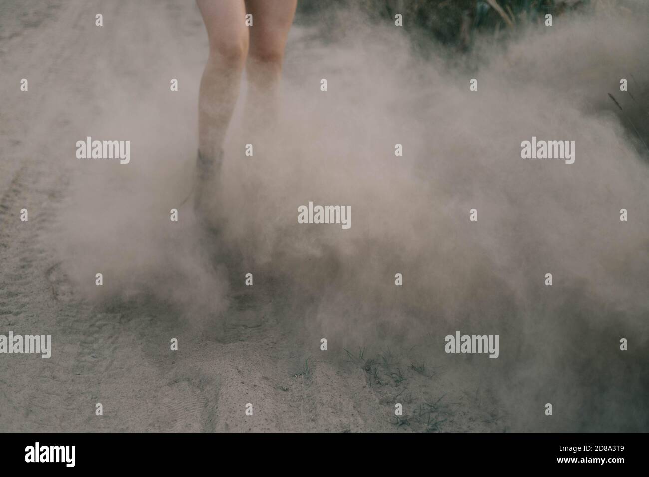 female legs jumping in the desert through fine dust carrying clouds of ...
