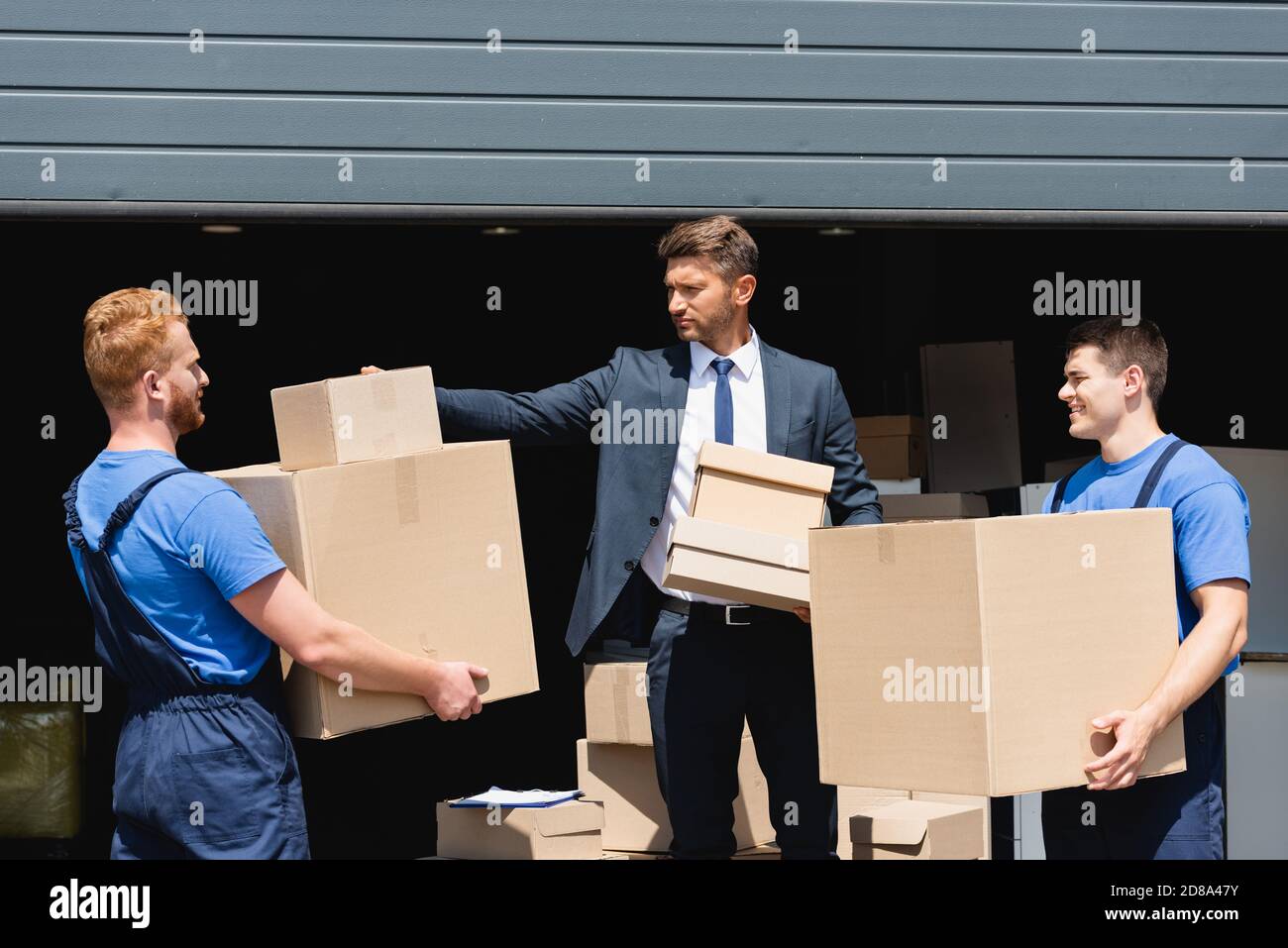 Businessman stacking cardboard boxes near loaders and warehouse ...