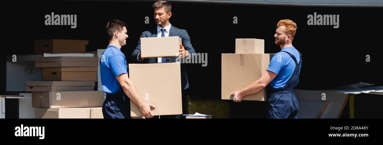 Horizontal crop of loaders holding carton boxes near businessman in ...