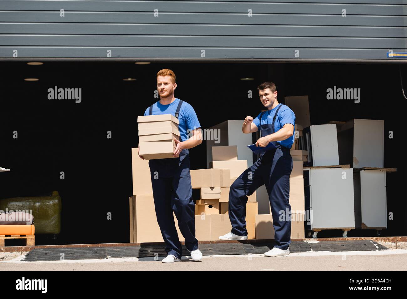Loader holding carton boxes near colleague with clipboard pointing with ...