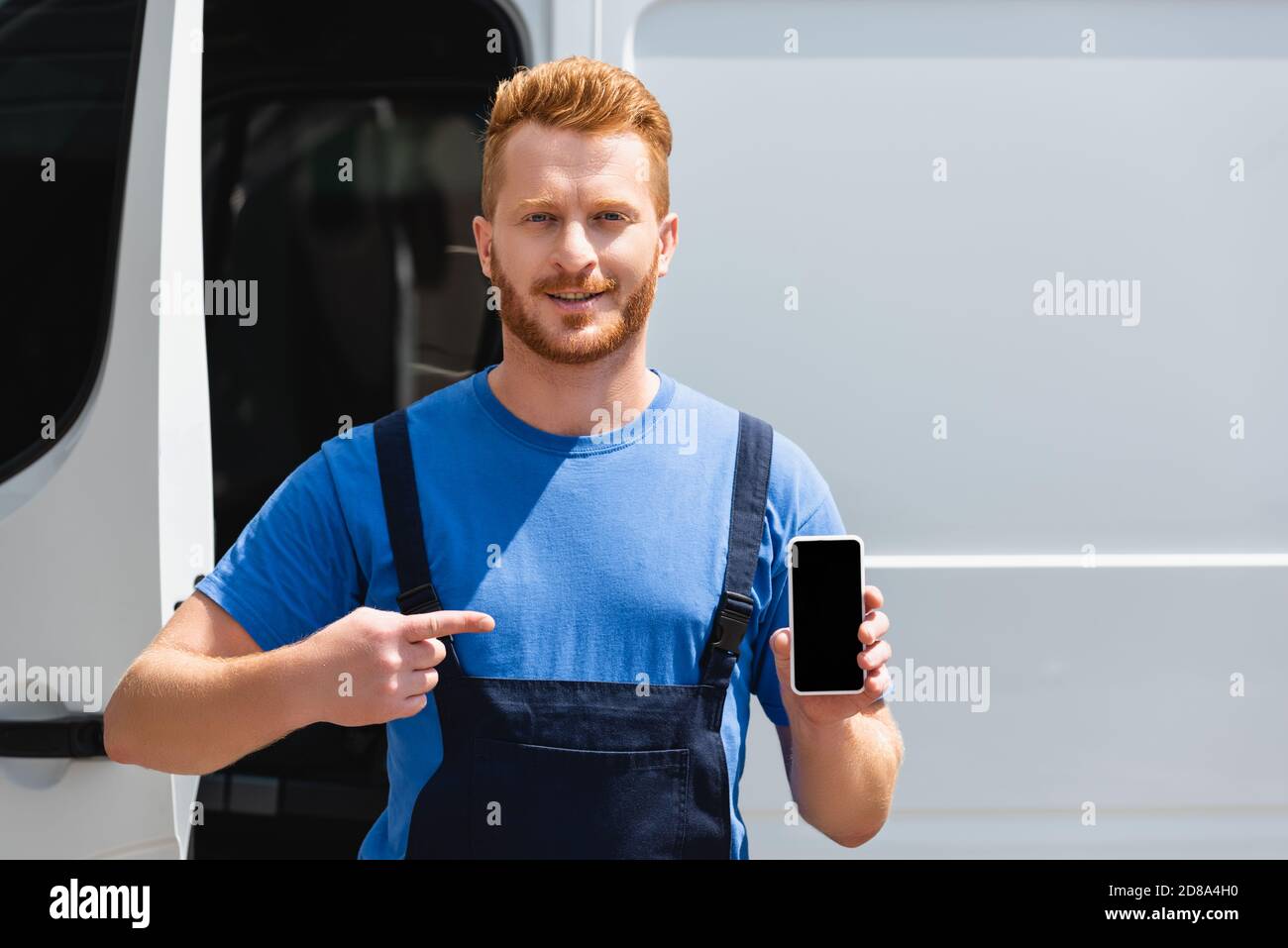 Loader in overalls pointing at smartphone with blank screen near truck ...