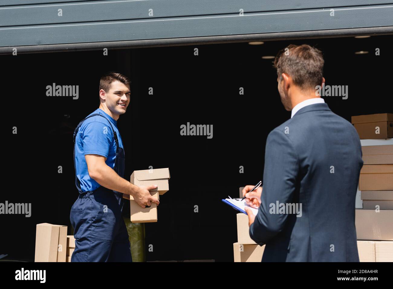 Selective focus of loader holding carton boxes near businessman writing ...