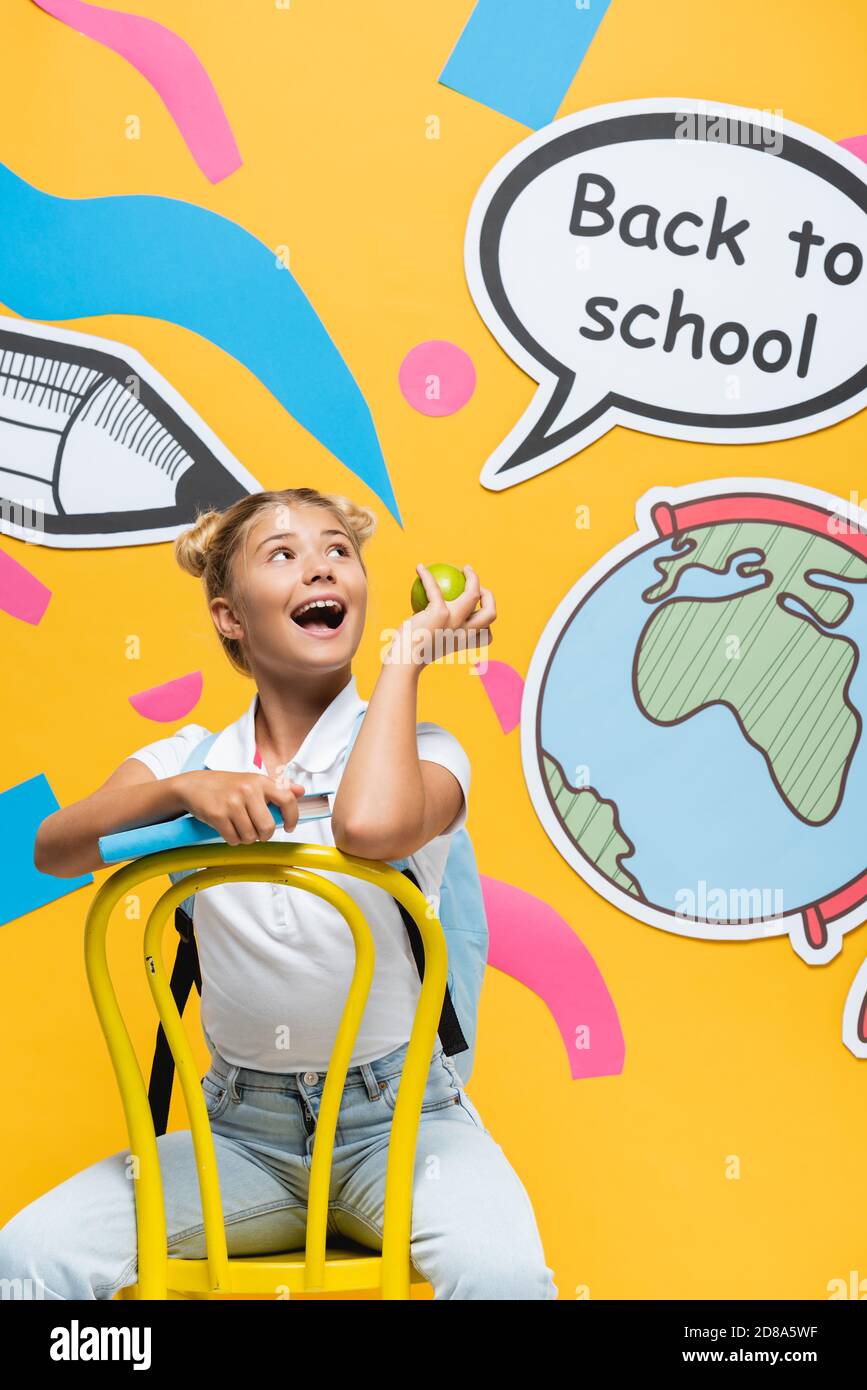 Excited kid with apple and book looking at speech bubble with back to ...