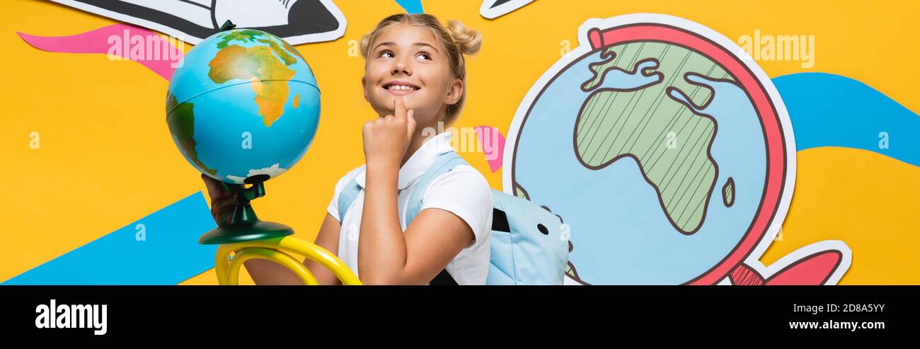 Panoramic shot of dreamy schoolkid with globe sitting near paper ...