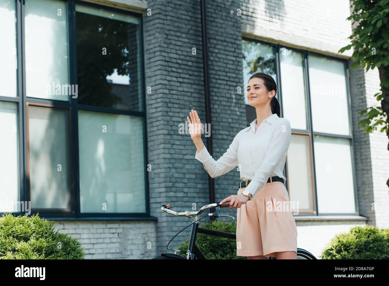 cheerful young businesswoman standing with bike and waving hand Stock ...