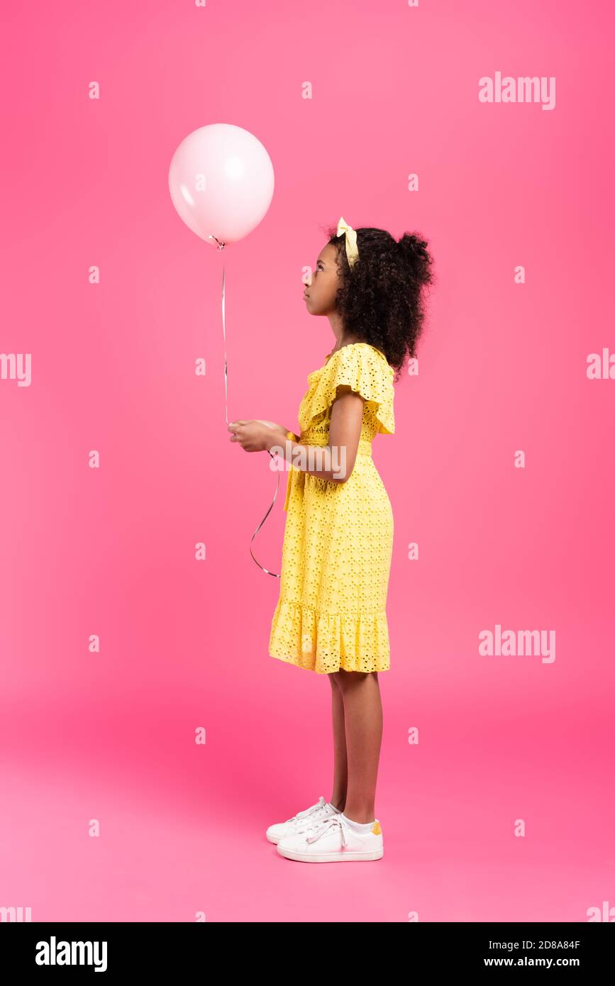 side view of curly african american child in yellow outfit with balloon ...