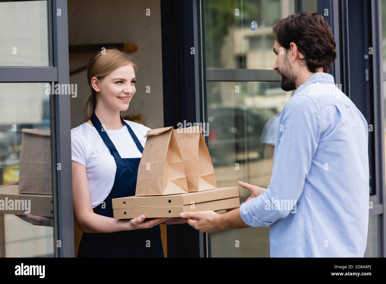 Attractive waitress giving pizza boxes and paper bags to man at entry ...