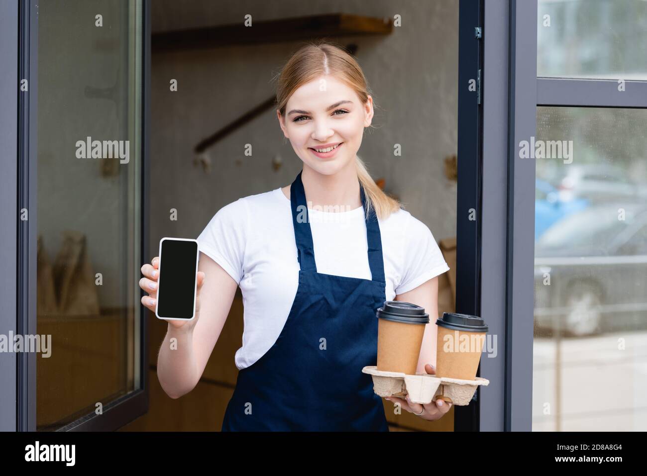 Front view of beautiful waitress holding smartphone and paper cups near ...