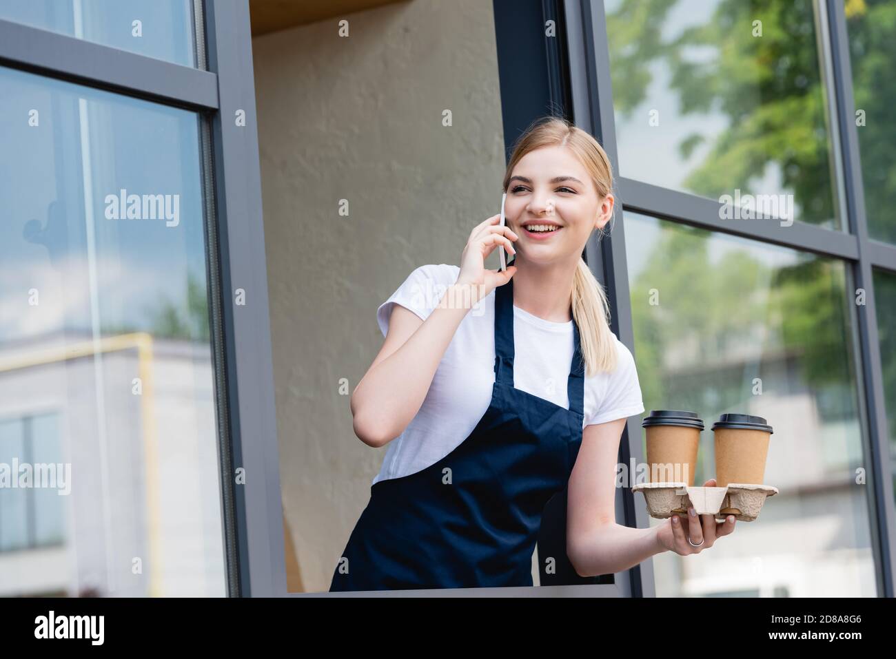 Low angle view of smiling waitress talking on smartphone and holding ...