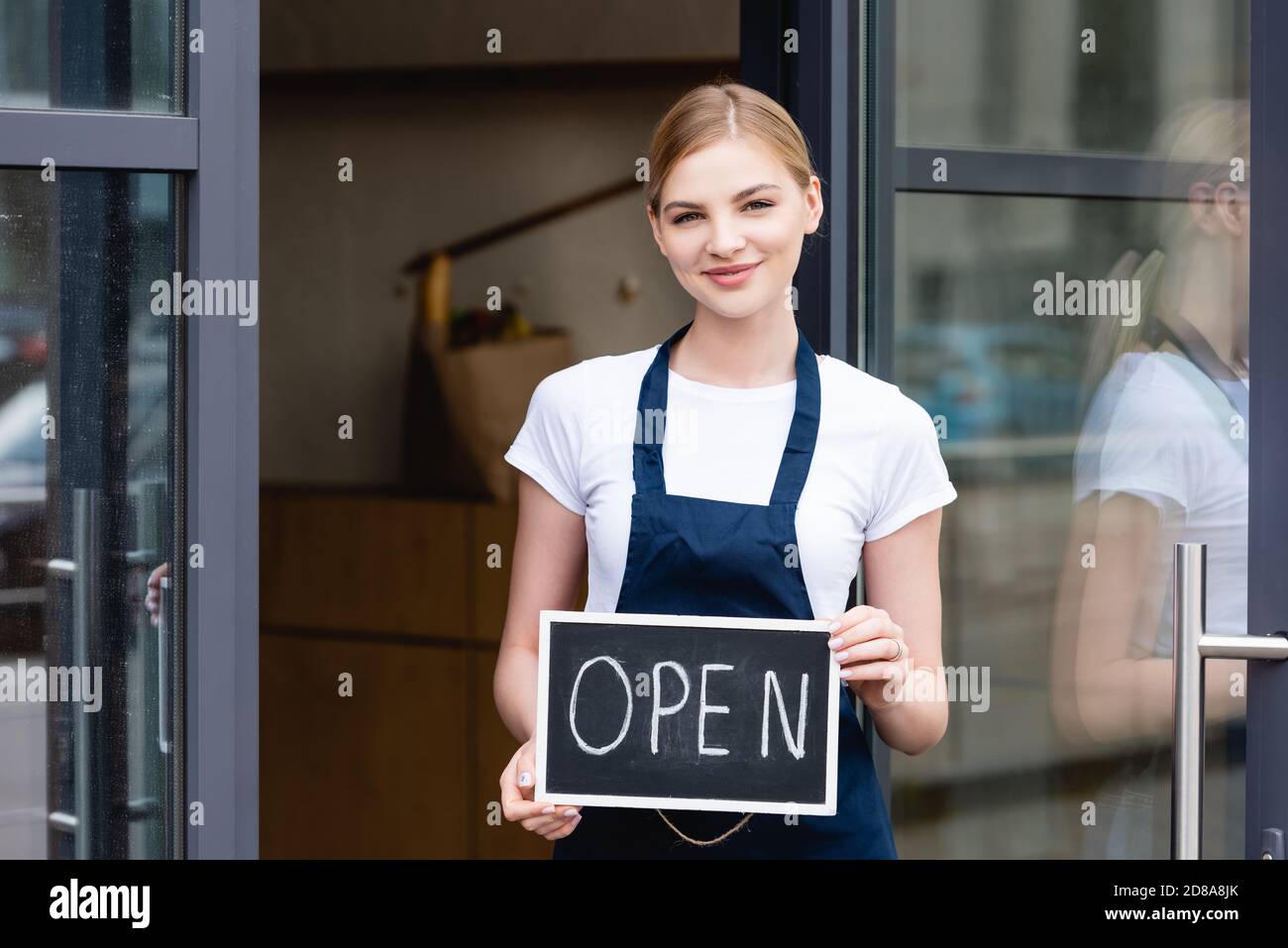 Smiling waitress holding signboard with open lettering near door of ...