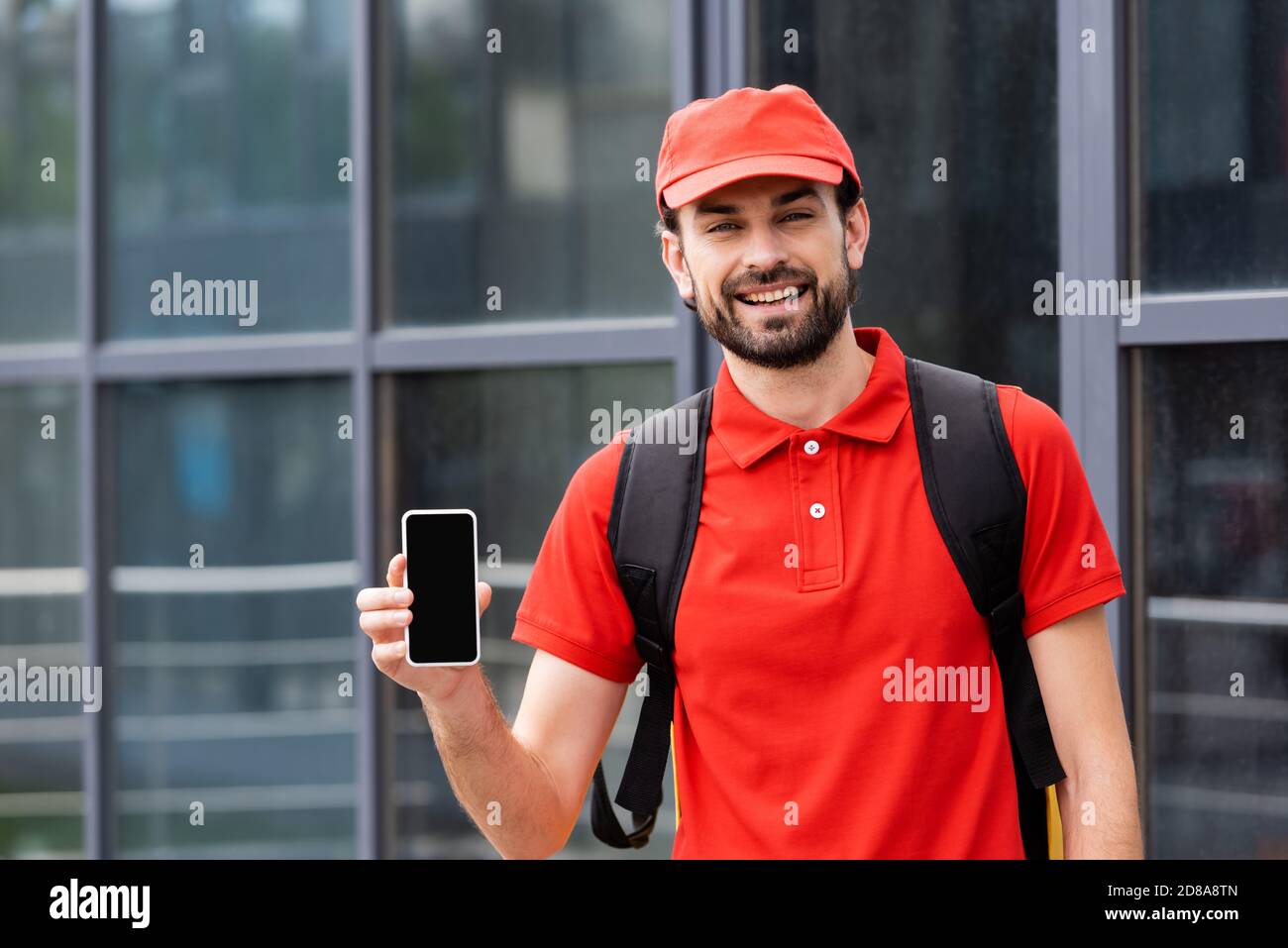 Handsome courier in uniform holding smartphone with blank screen on ...