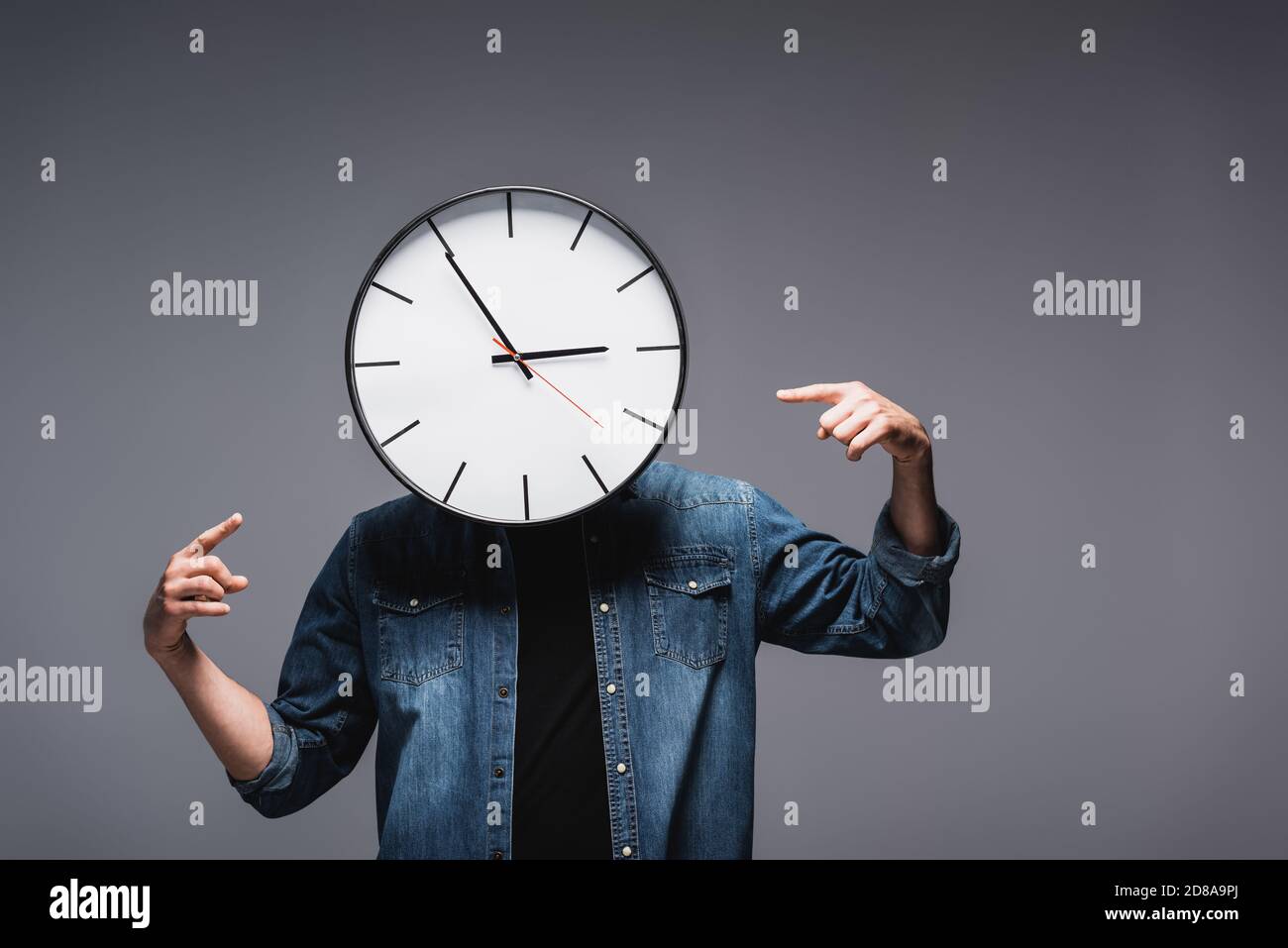 Man with clock near face pointing with fingers on grey background ...
