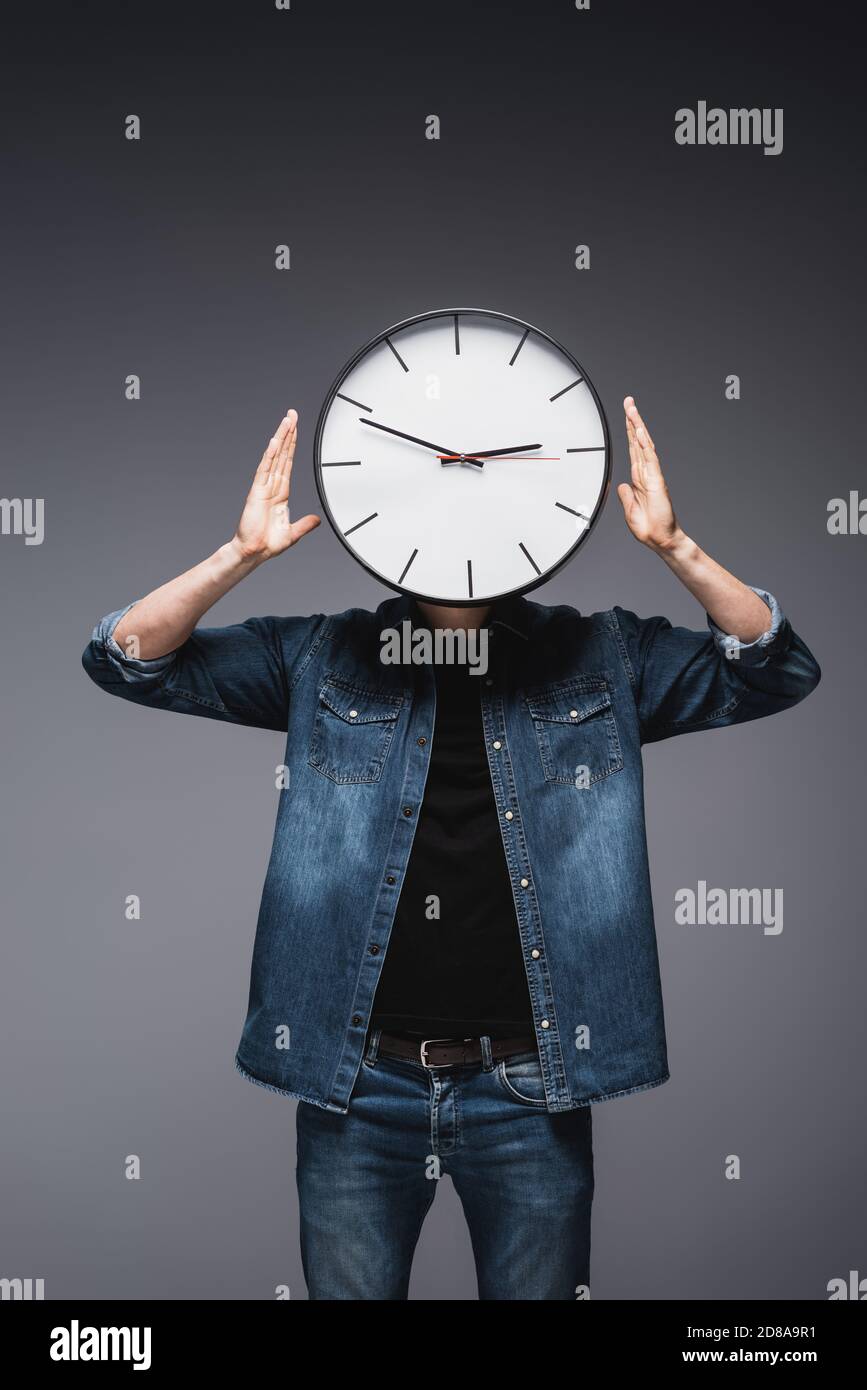 Young man in jeans jacket with clock on head on grey background ...