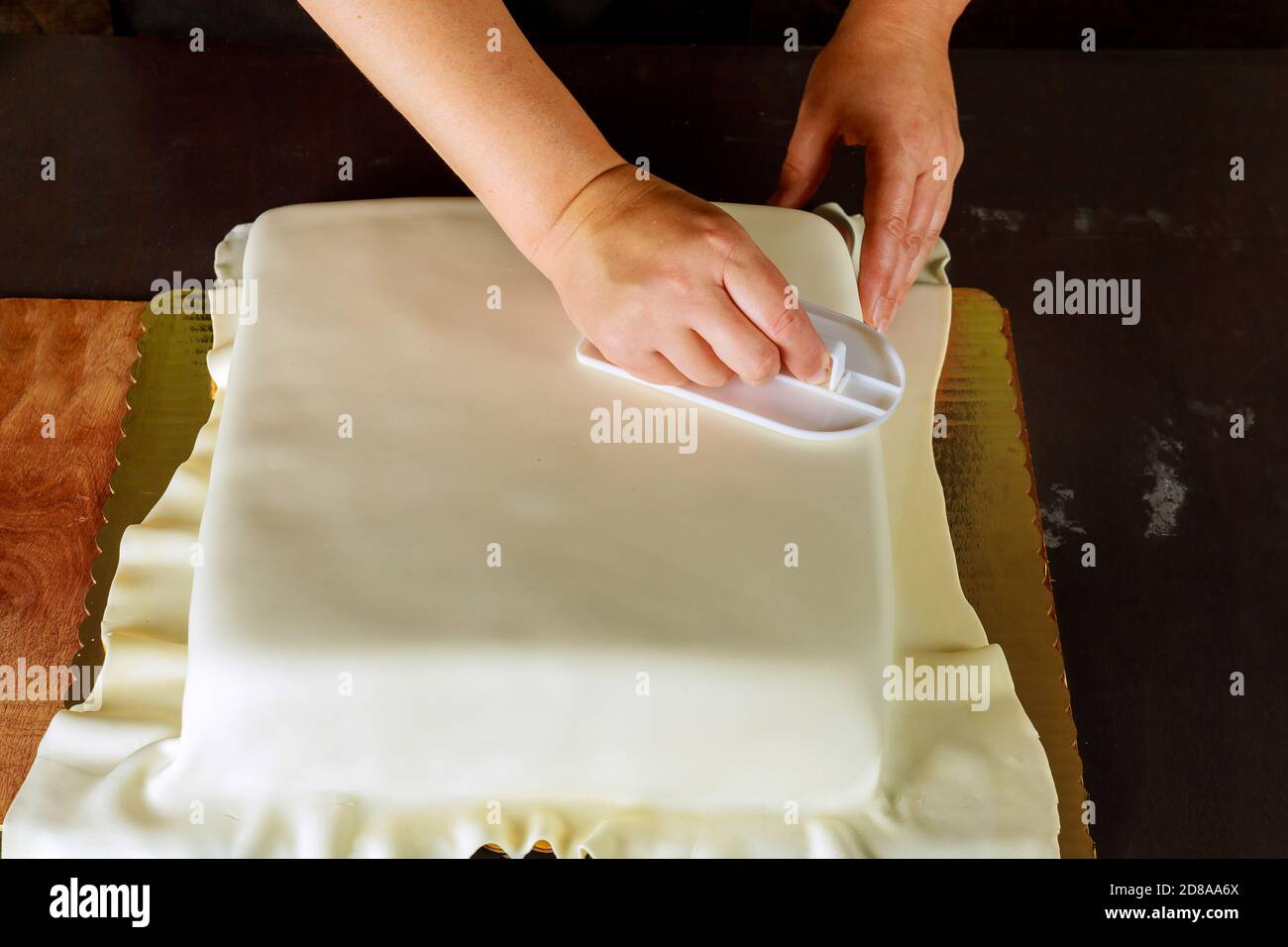 Woman decorating square cake with white fondant. Technique of making ...