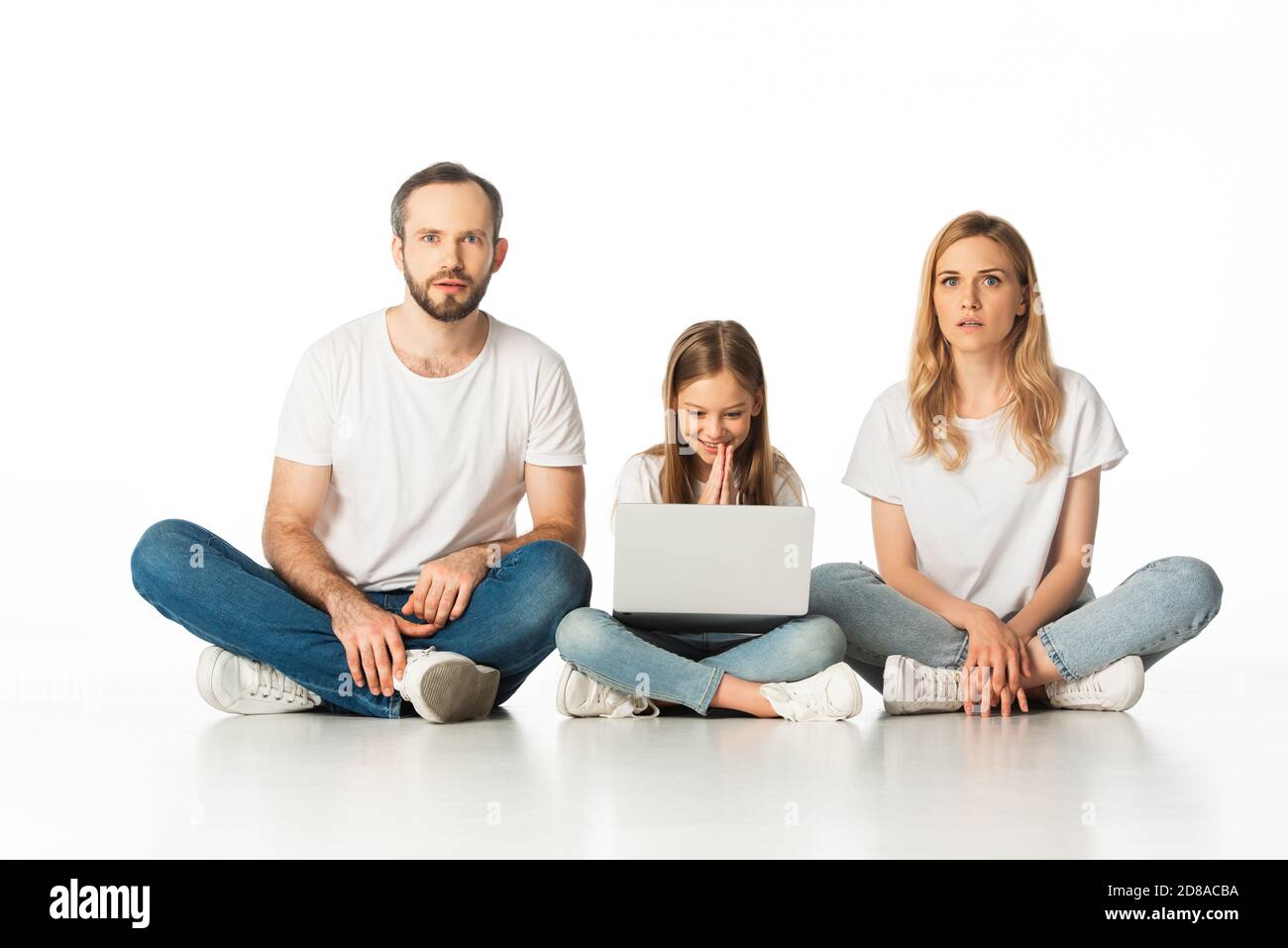 shocked parents sitting on floor near happy daughter with laptop ...