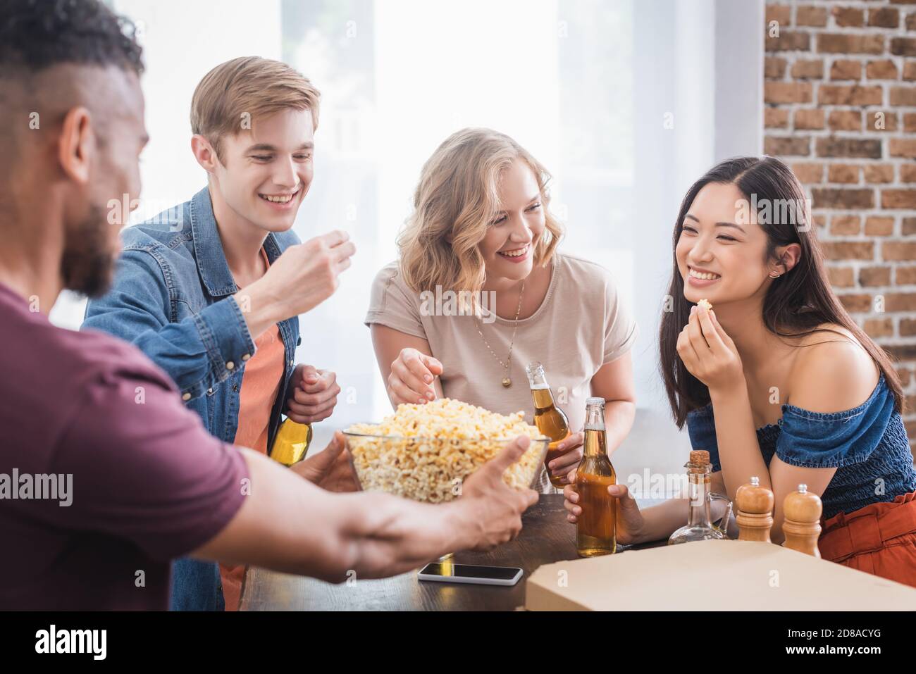 excited multiethnic friends eating popcorn and talking during party ...