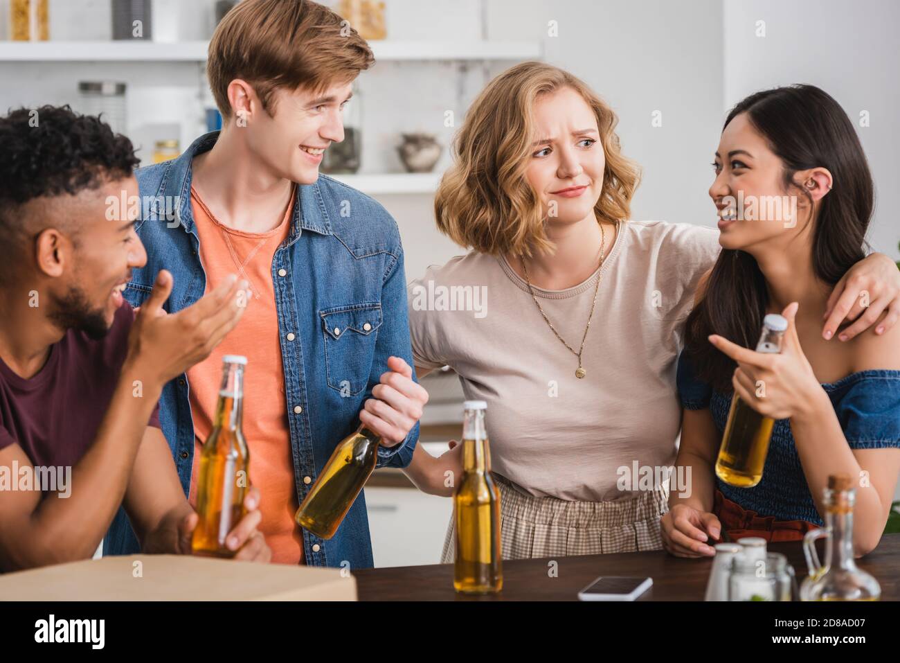 excited multicultural friends with bottles of beer talking during party ...