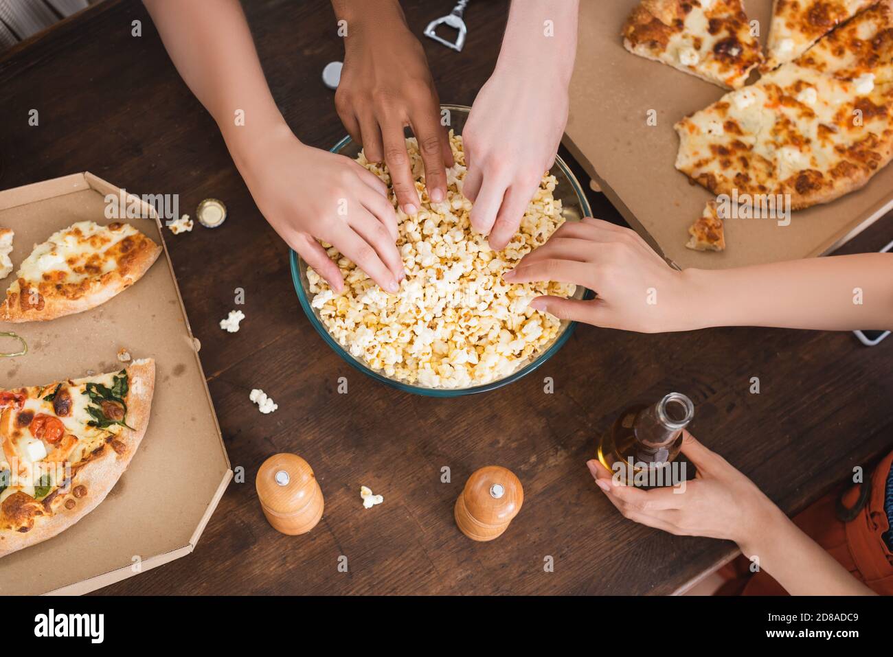 top view of multicultural friends taking popcorn from bowl during party ...