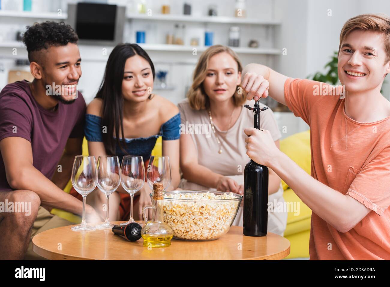 young man opening bottle of red wine near multicultural friends Stock ...