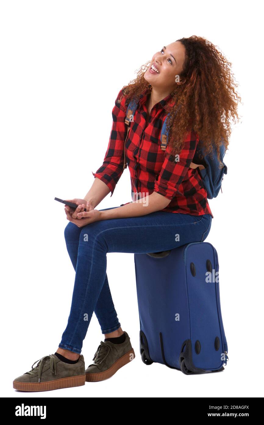 Portrait of happy young woman sitting on suitcase against isolated ...
