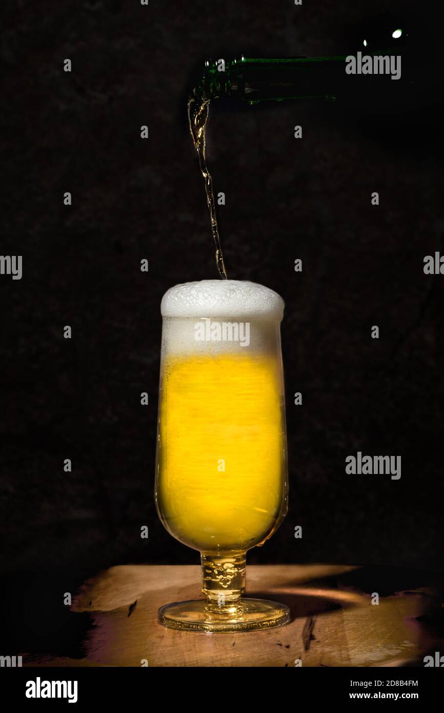 Glass bottle pouring beer on a glass making foam, golden color, against ...