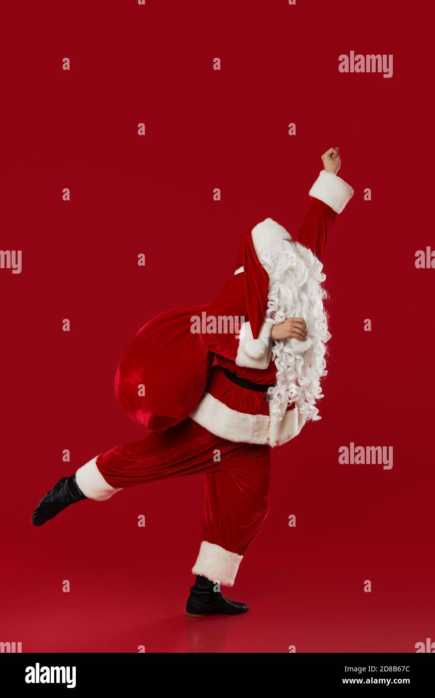 Joyful Santa Claus in super hero pose jumps high with gifts on red ...