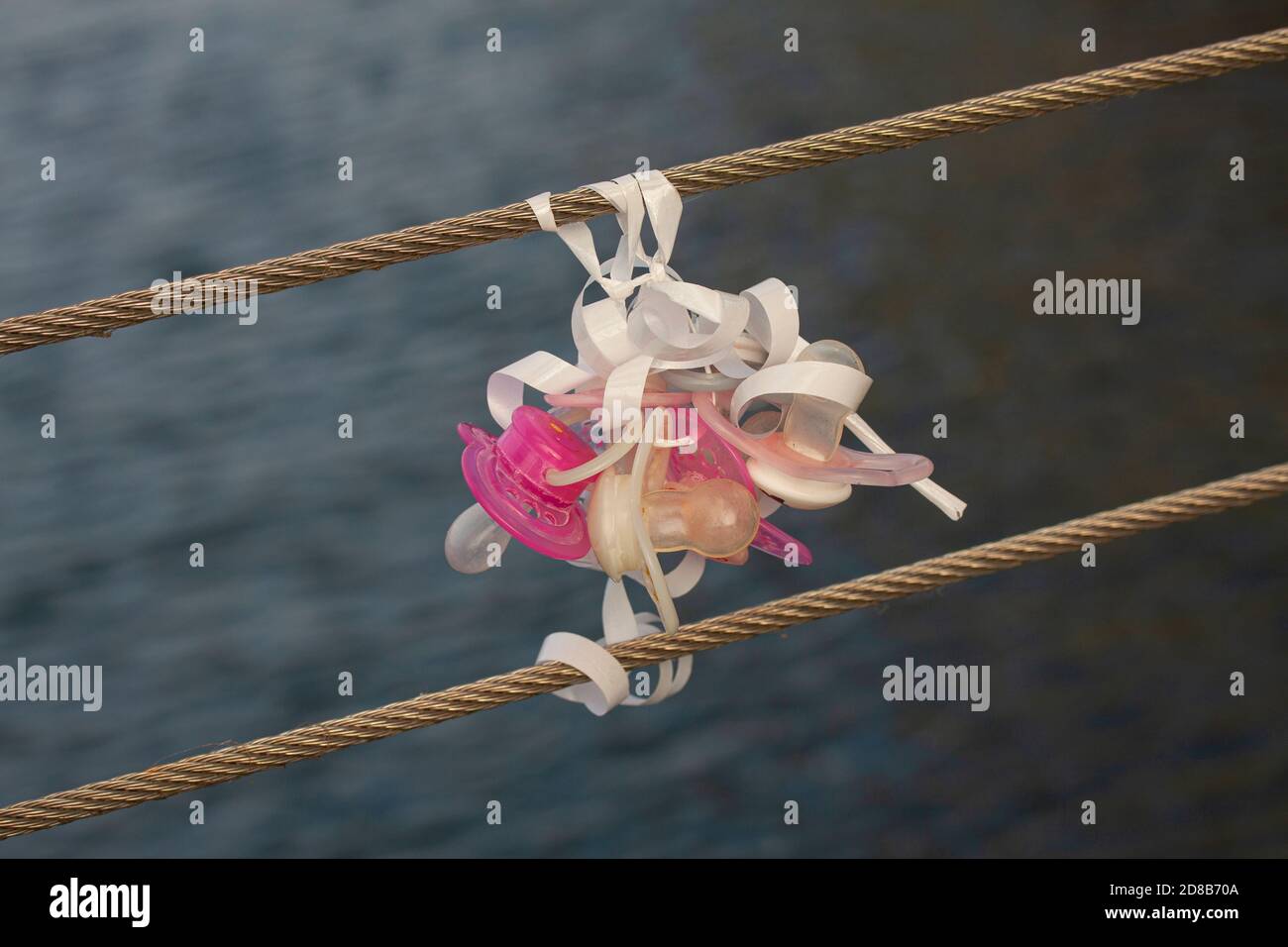 Bunch of baby pacifiers fixed to a railing wire on a bridge. Hanging ...