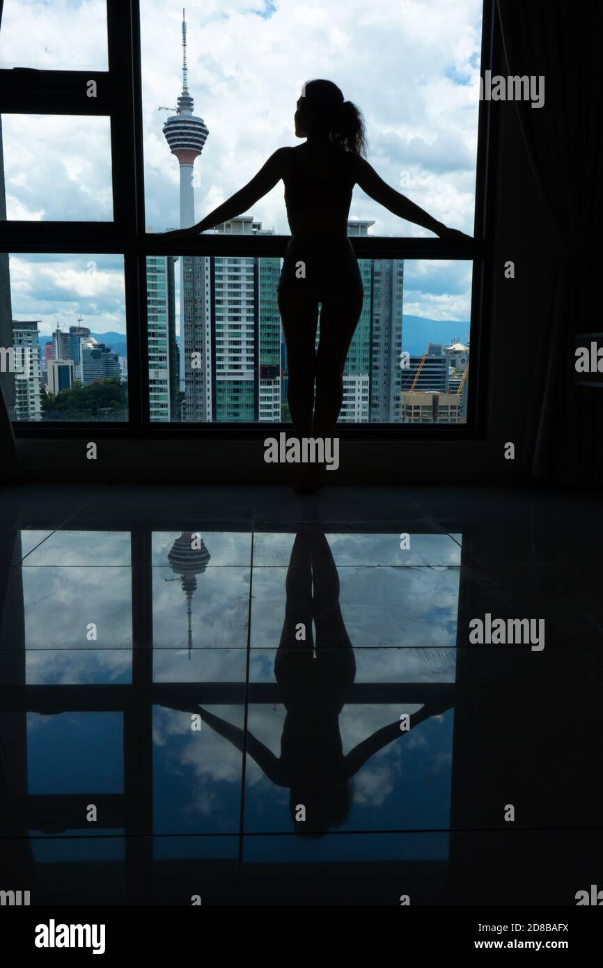A slender girl is looking at the city through a large window. High ...
