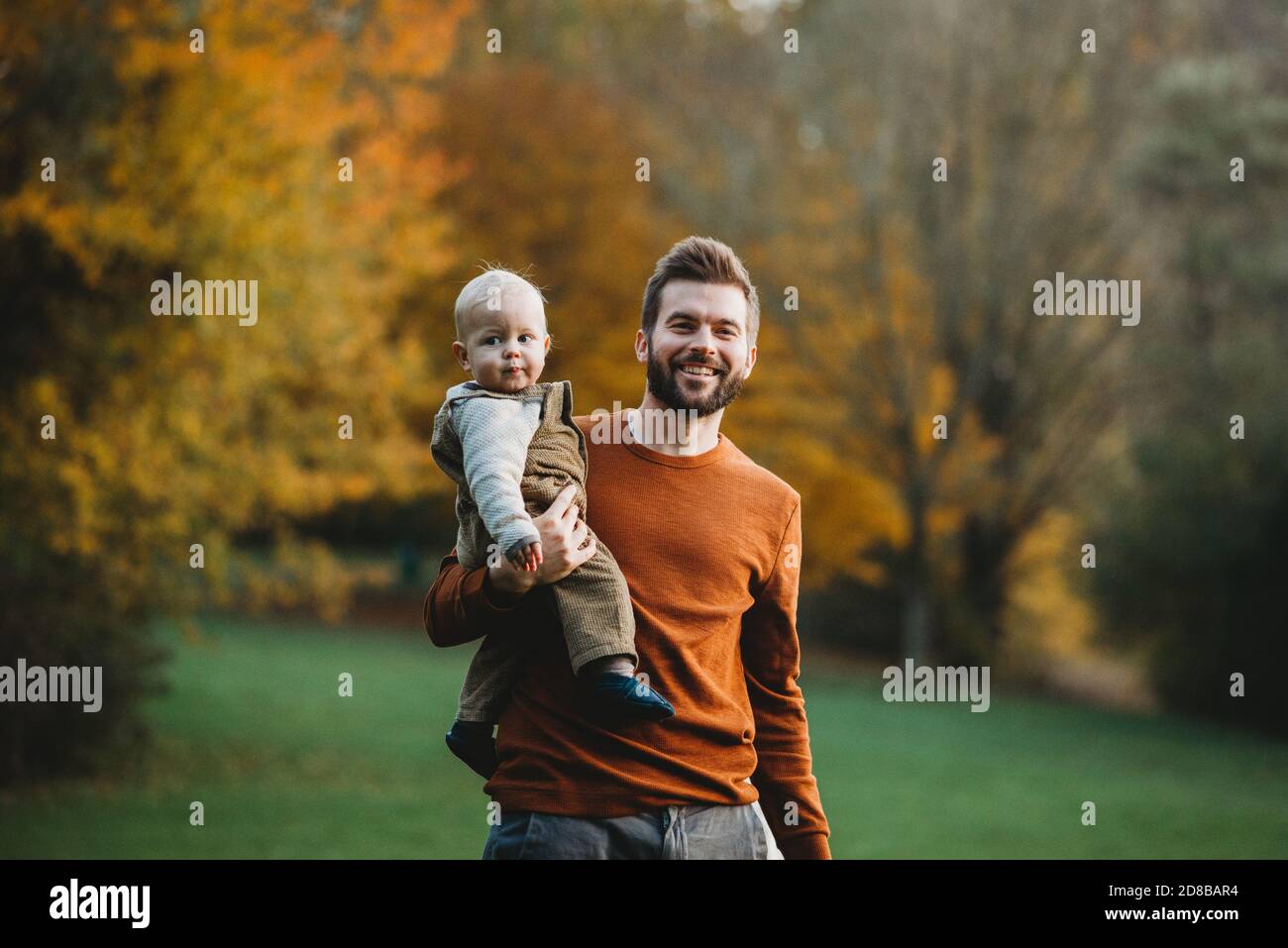 Father and son smiling at the park in a Fall day wearing earth tones ...