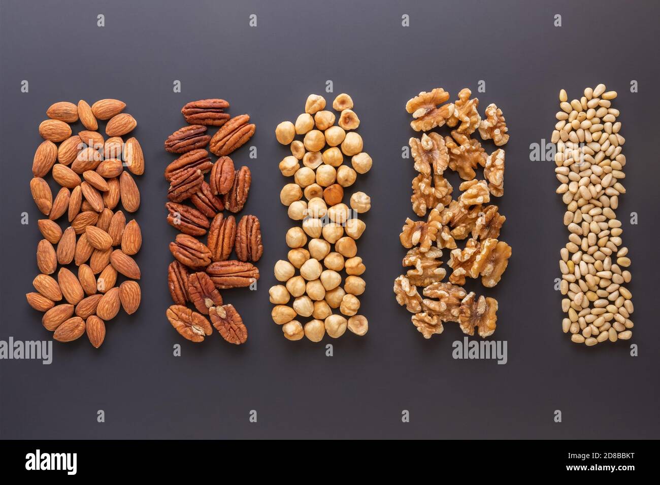 almond, pine, pecan nuts, walnuts, hazelnuts in stacks on a grey table ...