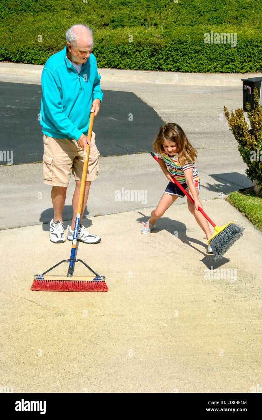 A grandfather and granddaughter share driveway sweeping chores in a ...