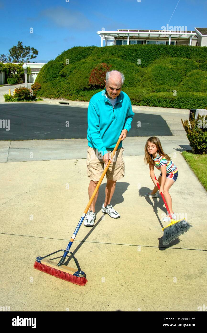 A grandfather and granddaughter share driveway sweeping chores in a ...