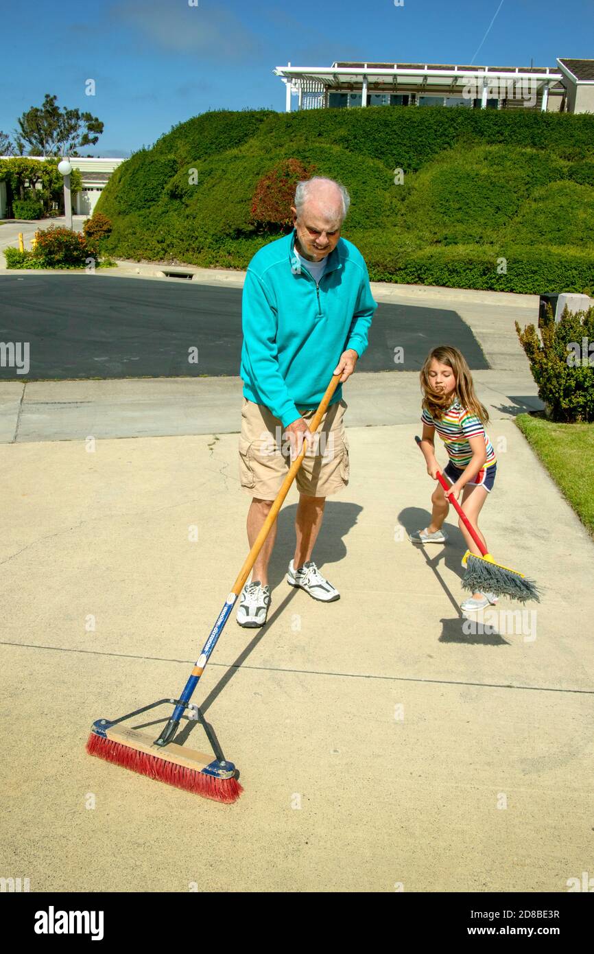 A grandfather and granddaughter share driveway sweeping chores in a ...