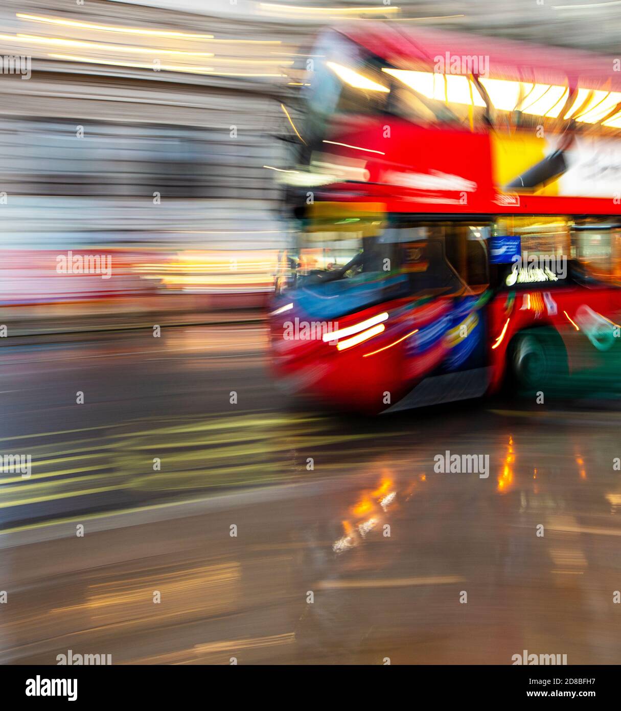 Red London bus moving fast along Piccadilly; rainy afternoon, wet ...