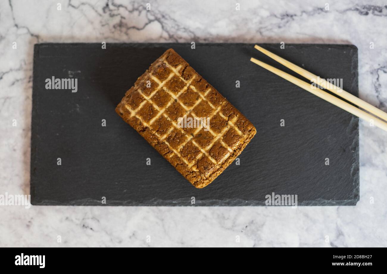 Top view of a piece of smoked tofu with sesame seeds on a slate board ...