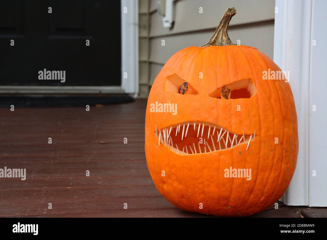 A jack-o-lantern with toothpicks for teeth on the front porch of a home ...