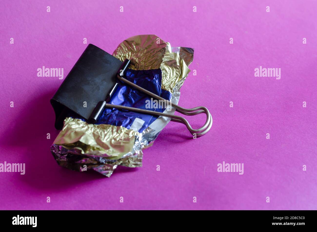 Smashed candy wrappers and Metal black Binder Clip on purple background ...