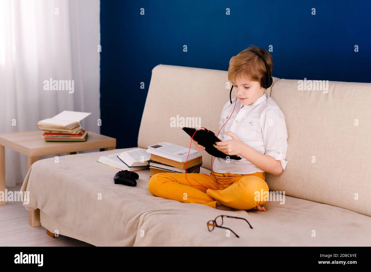 A boy with glasses and headphones is learning lessons with a tablet and ...