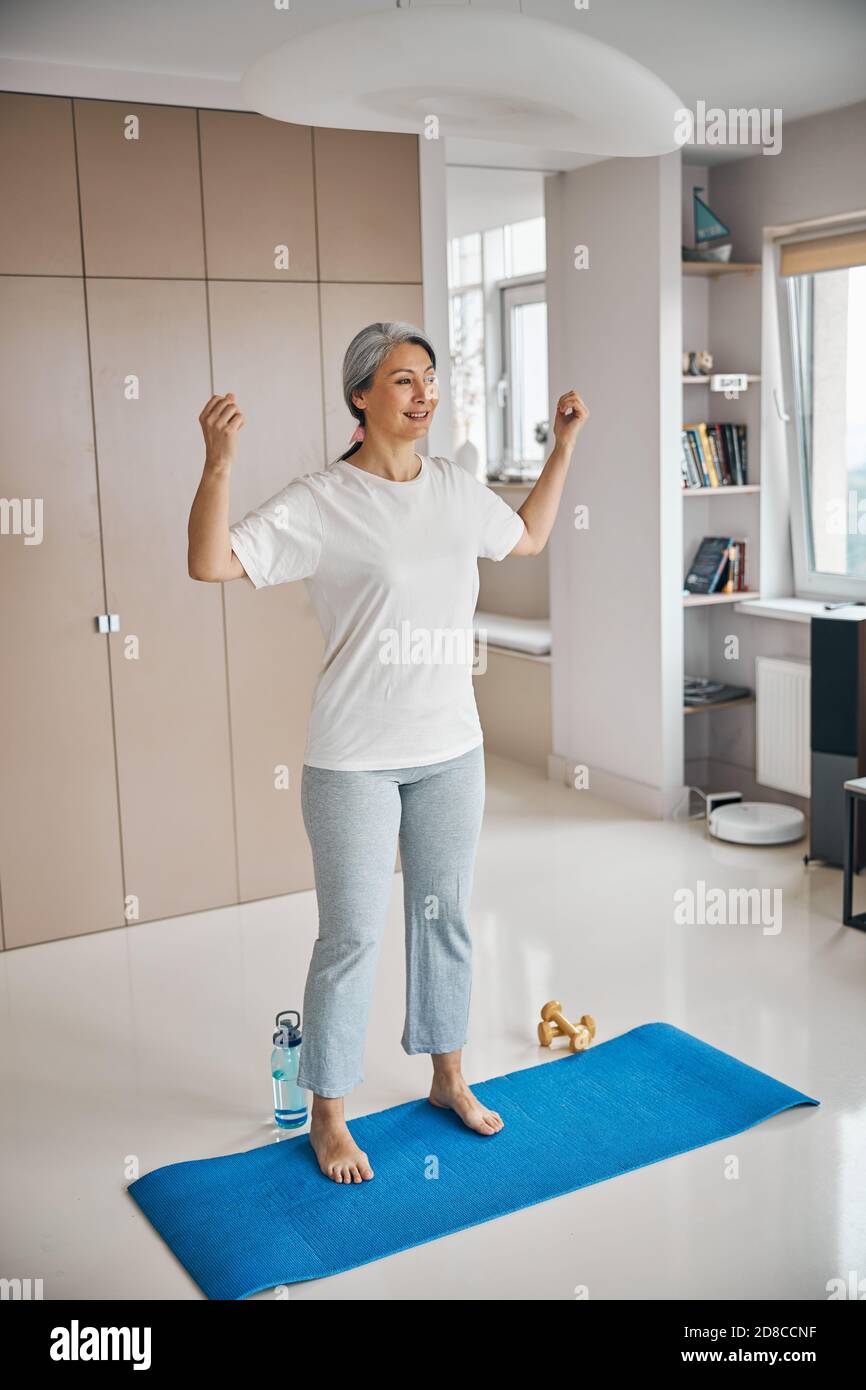 Beautiful sporty female putting her hands up while standing in living ...