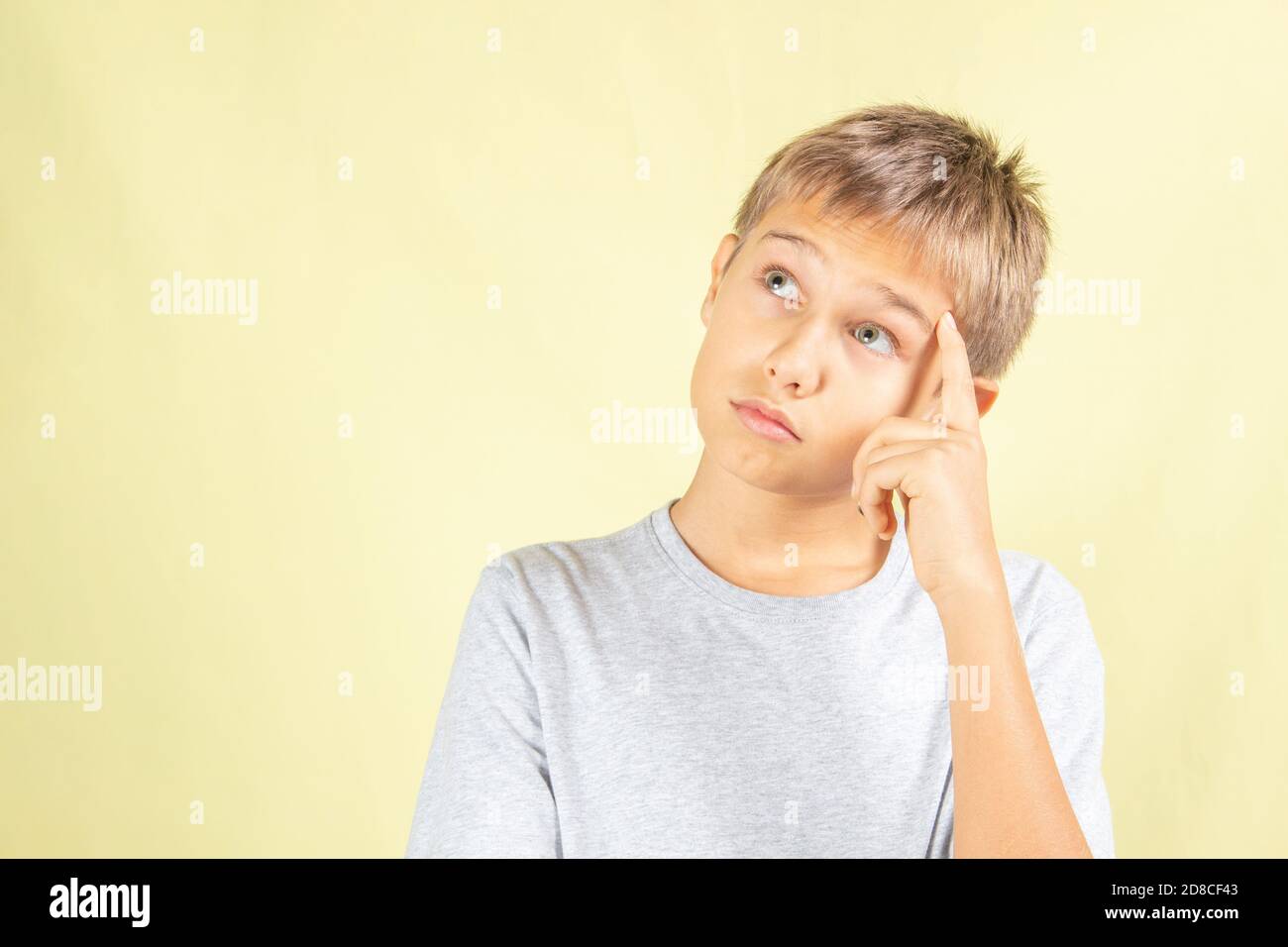 Thinking young boy standing over light yellow background Stock Photo ...