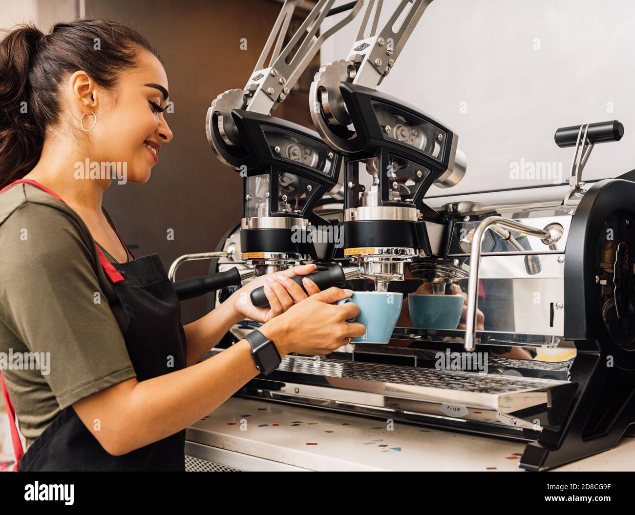 Female barista using a coffee machine. Smiling woman pouring hot coffee ...