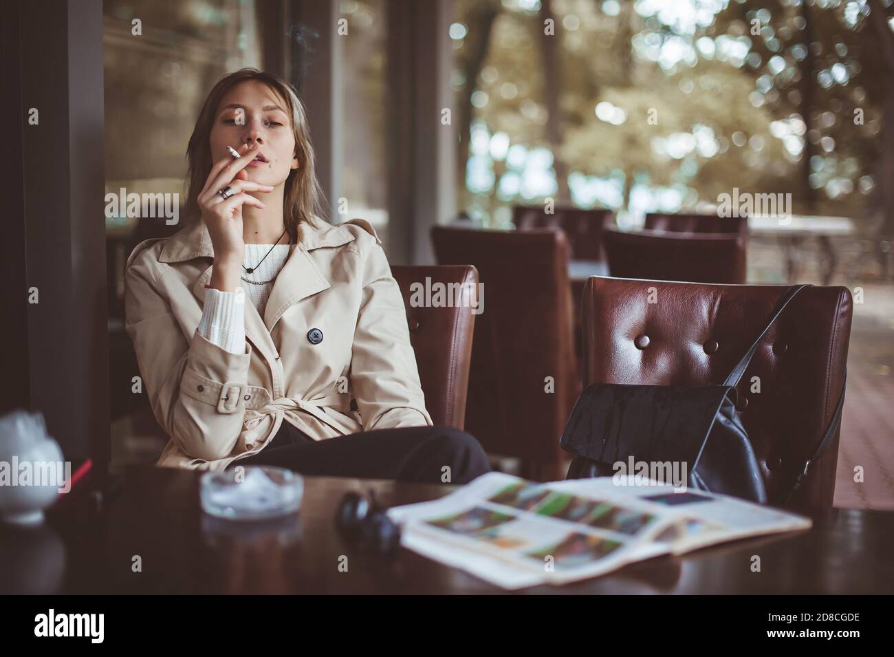 Beautiful woman sitting alone in cafeteria, smoking a cigarette and ...