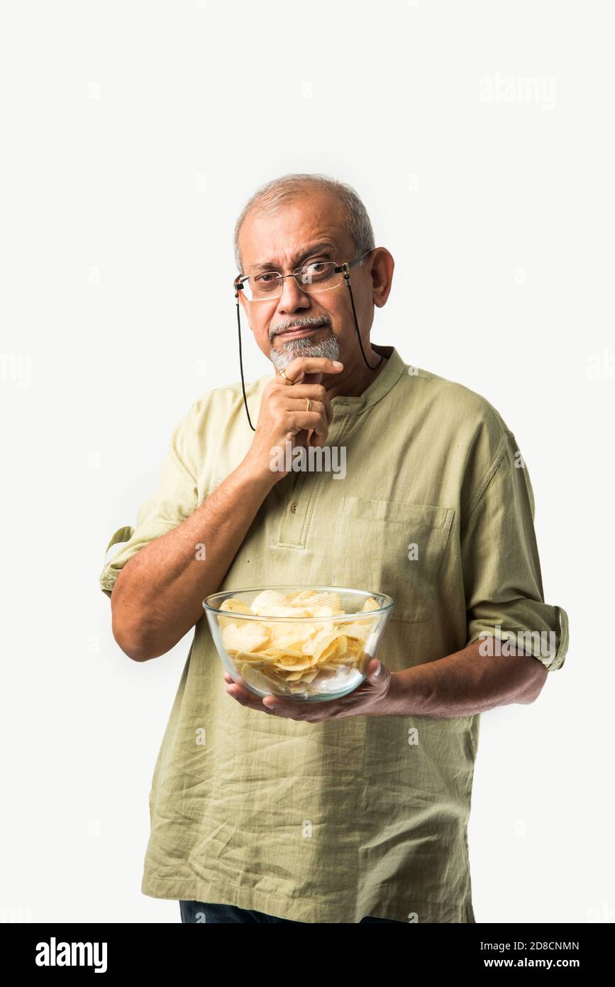 Indian asian old or retired senior man eating potato chips on white ...