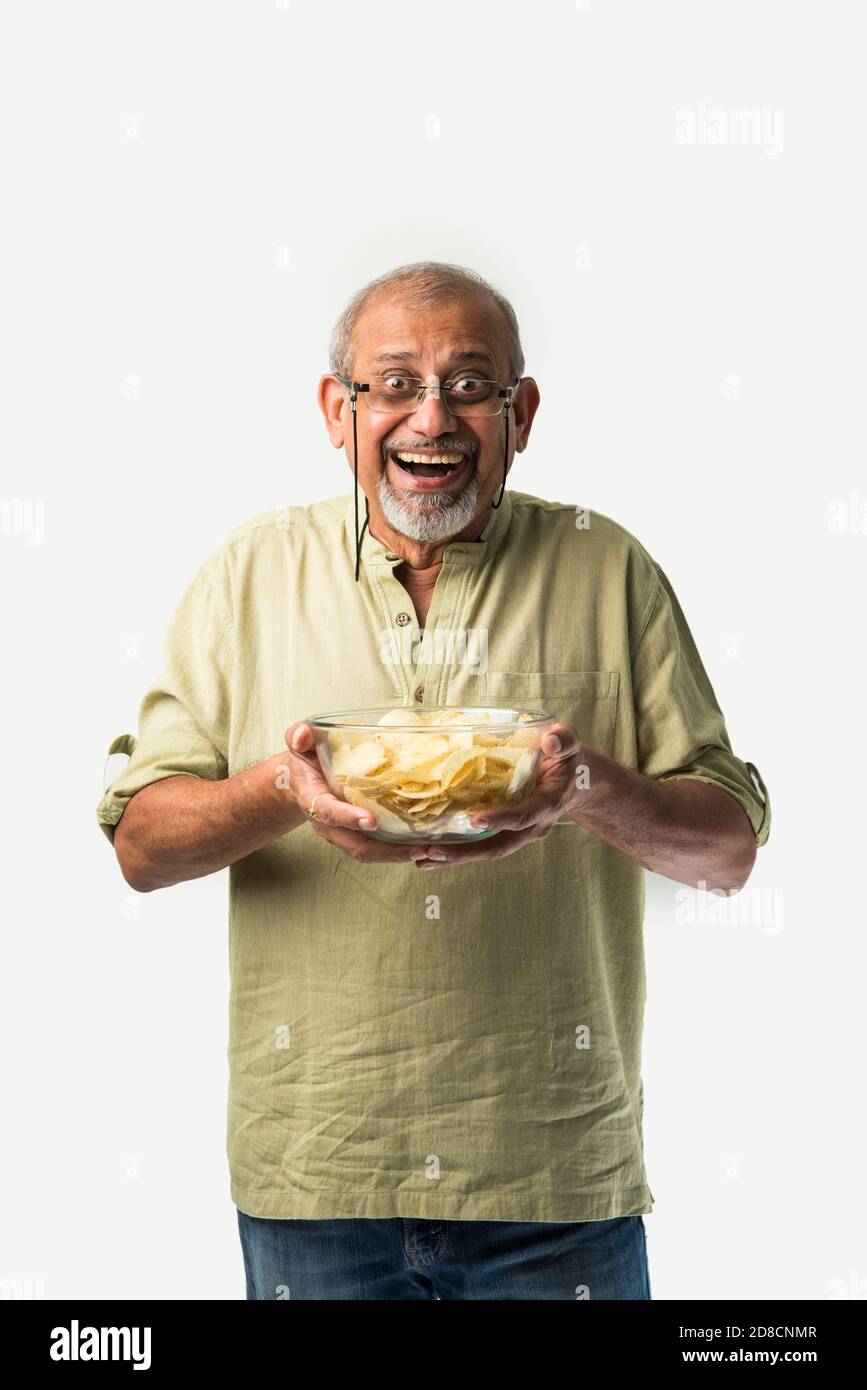 Indian asian old or retired senior man eating potato chips on white ...
