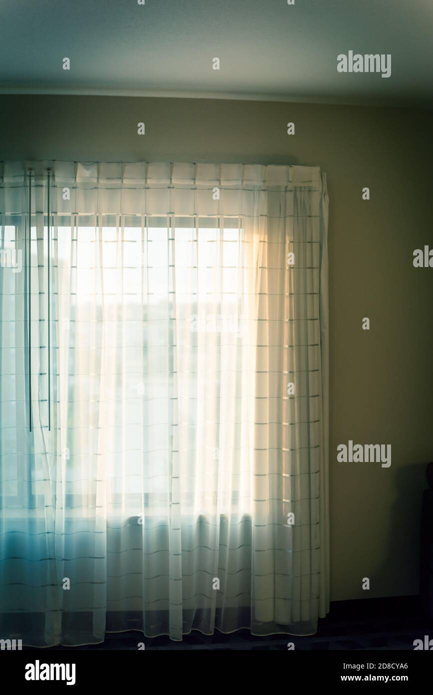 Hotel room with white curtain, drapery baton and backlit morning light ...