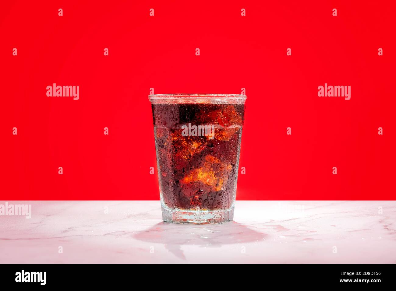 Ice cold glass of soda, fizzy drink, cola, pop with ice cubes and condensation on a red ...