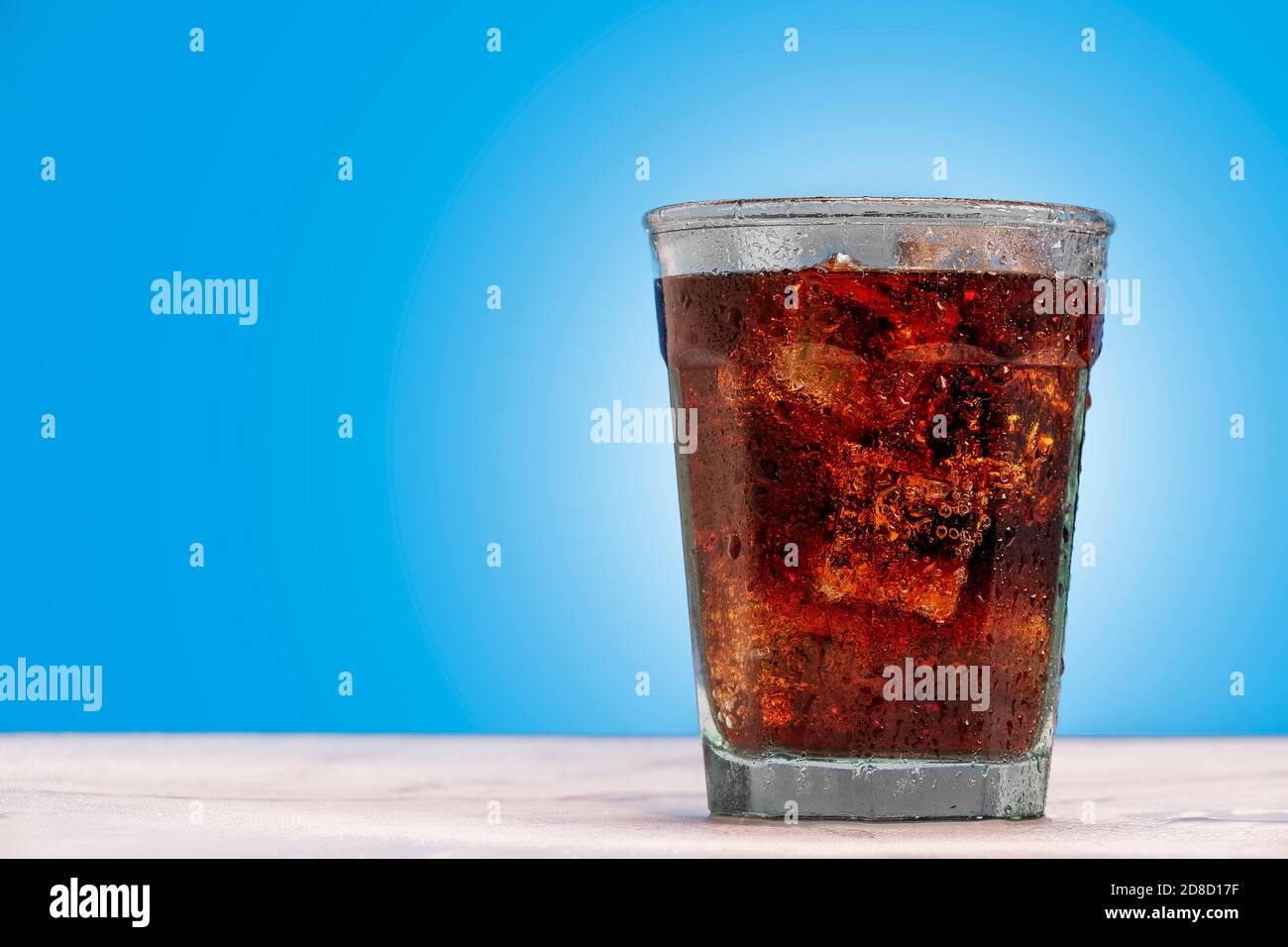 Ice cold glass of soda, fizzy drink, pop on a blue background with condensation and ice cubes ...