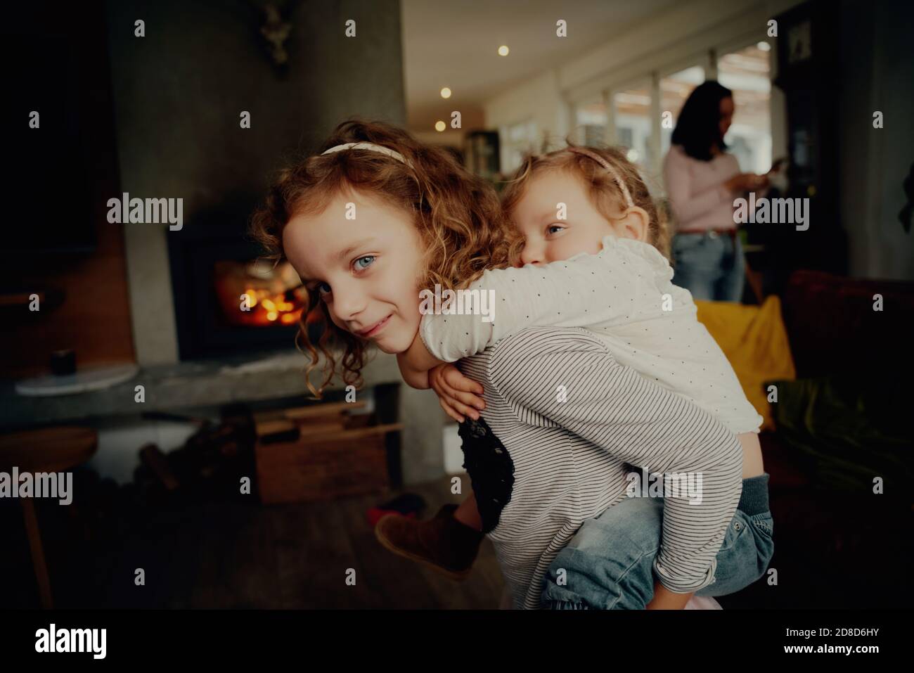 Cute little girl giving younger sister a piggyback ride at home Stock ...
