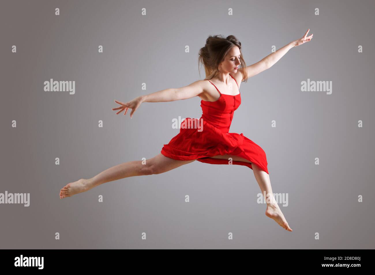 Portrait of elegant female dancer in red dress jumping against gray ...