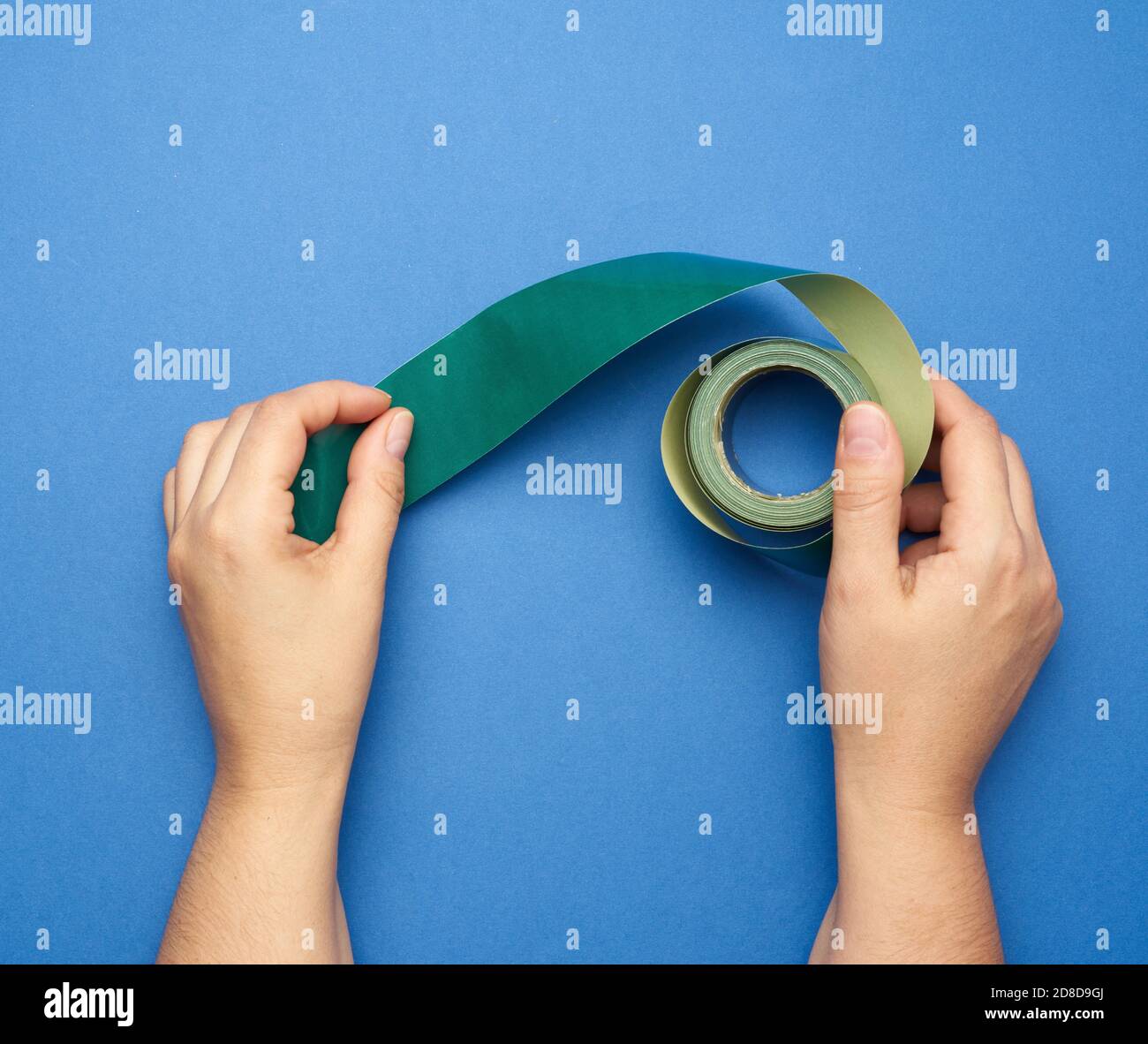 hand hold green rolled paper sticky tape on a bluebackground, top view ...